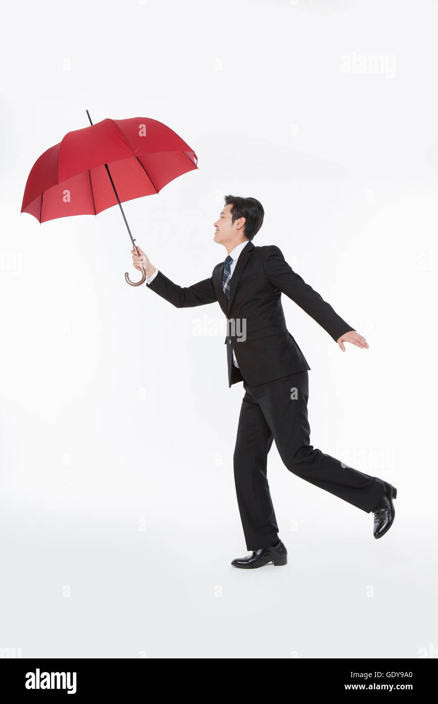 Side view of business man with a red umbrella standing on one foot ...
