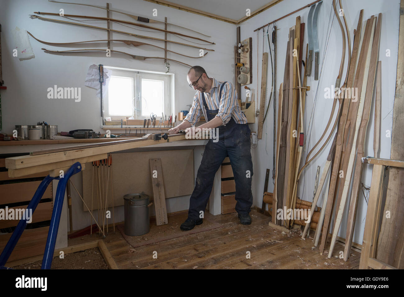 Male bow maker shaving wood and giving it a shape of bow in workshop ...