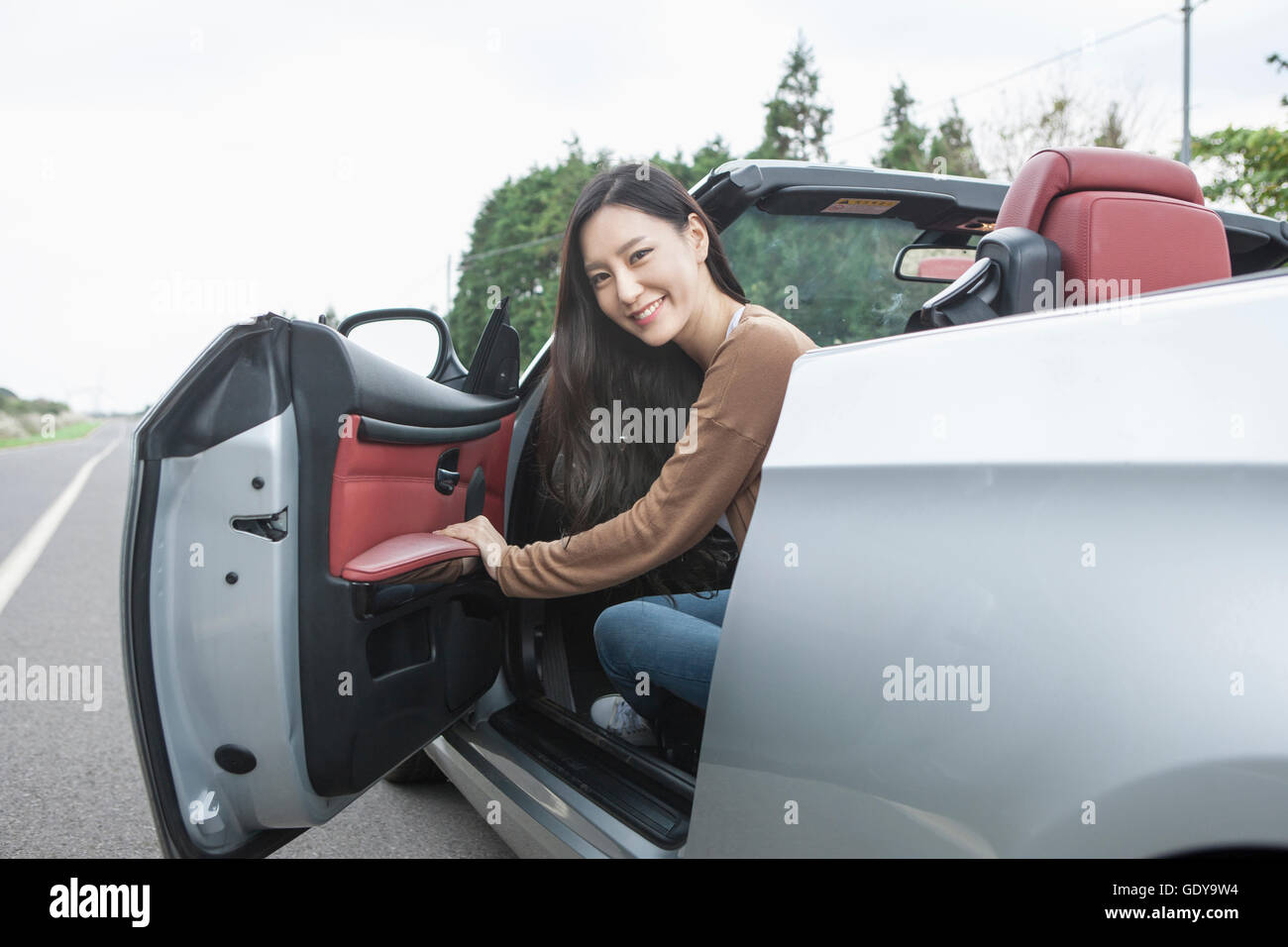 Side view of young smiling woman sitting in a car staring at front ...