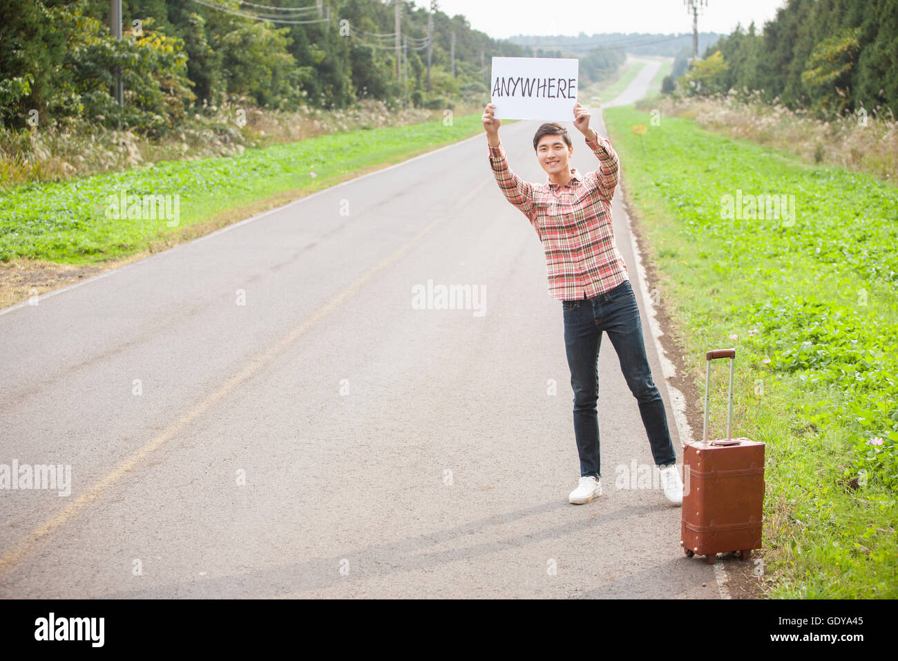 Young smiling travler standing holding message of ANYWHERE on roadside ...