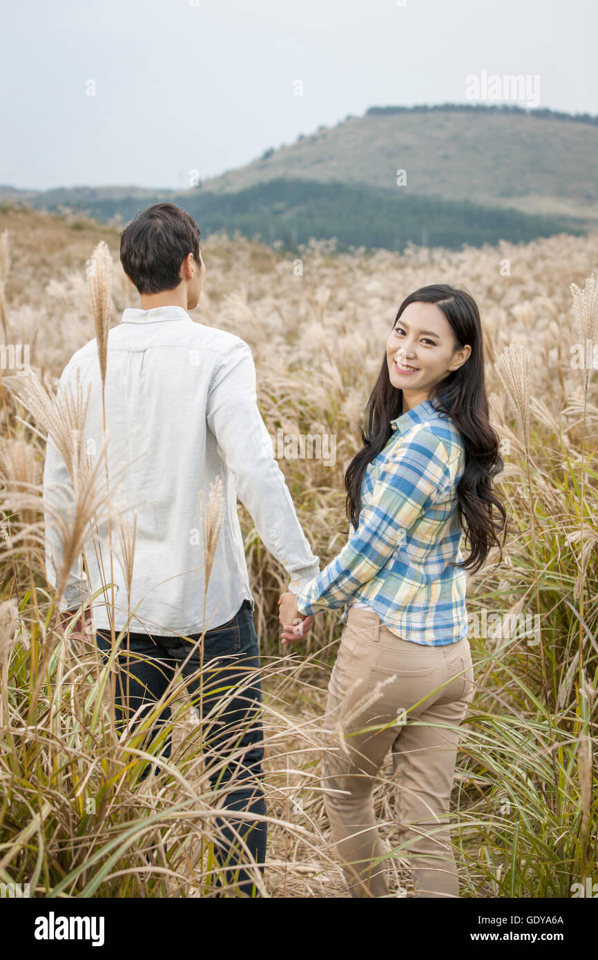 Back of young smiling woman looking back walking hand in hand with a ...