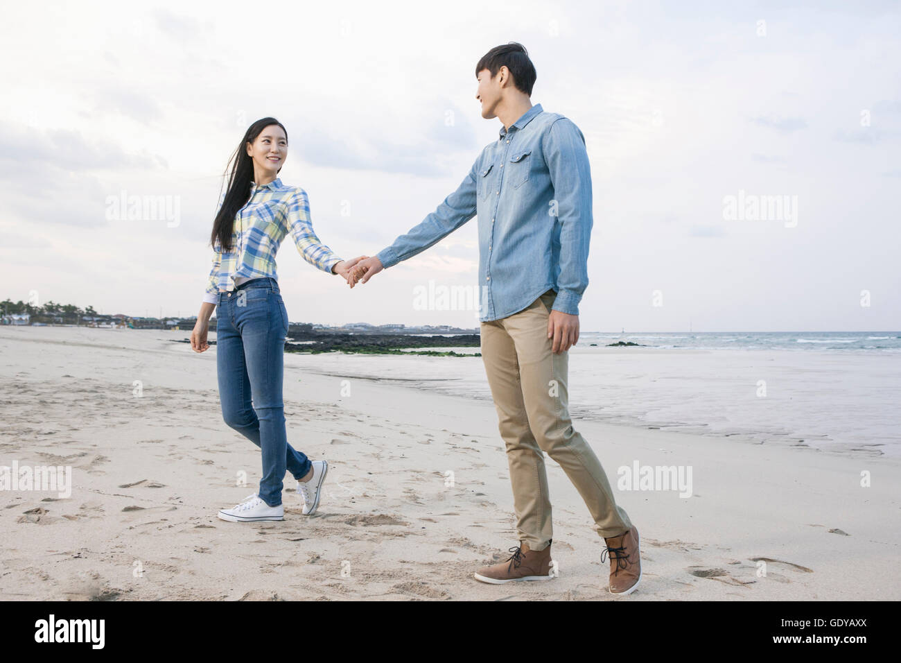 Side view of young smiling couple walking hand in hand at beach face to ...