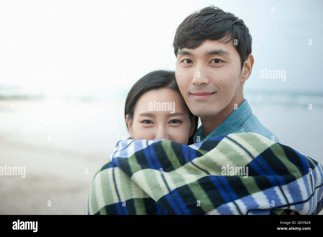 Portrait of young smiling couple sharing a blanket Stock Photo - Alamy
