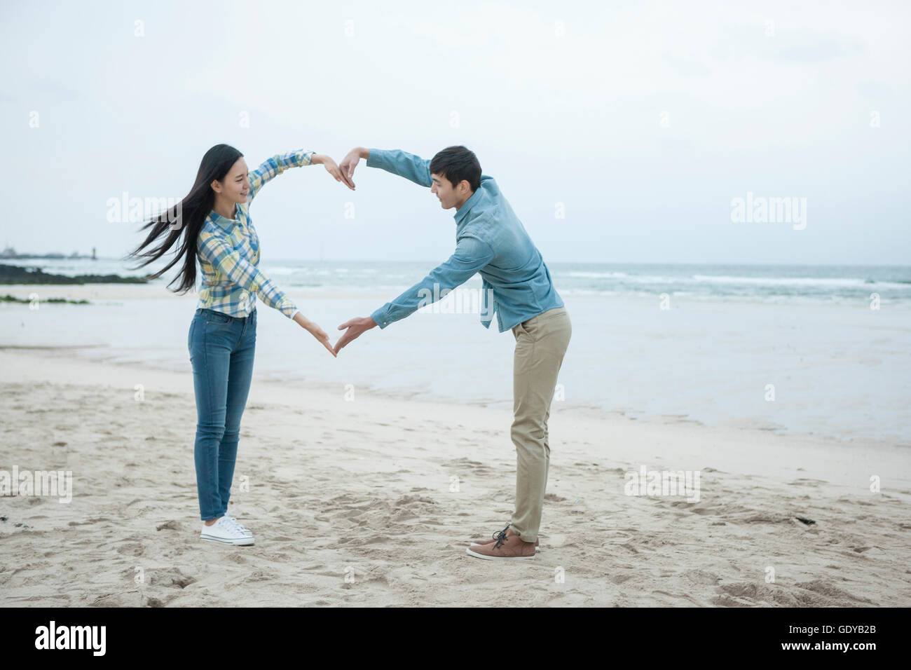 Side view of young smiling couple standing face to face making a heart ...
