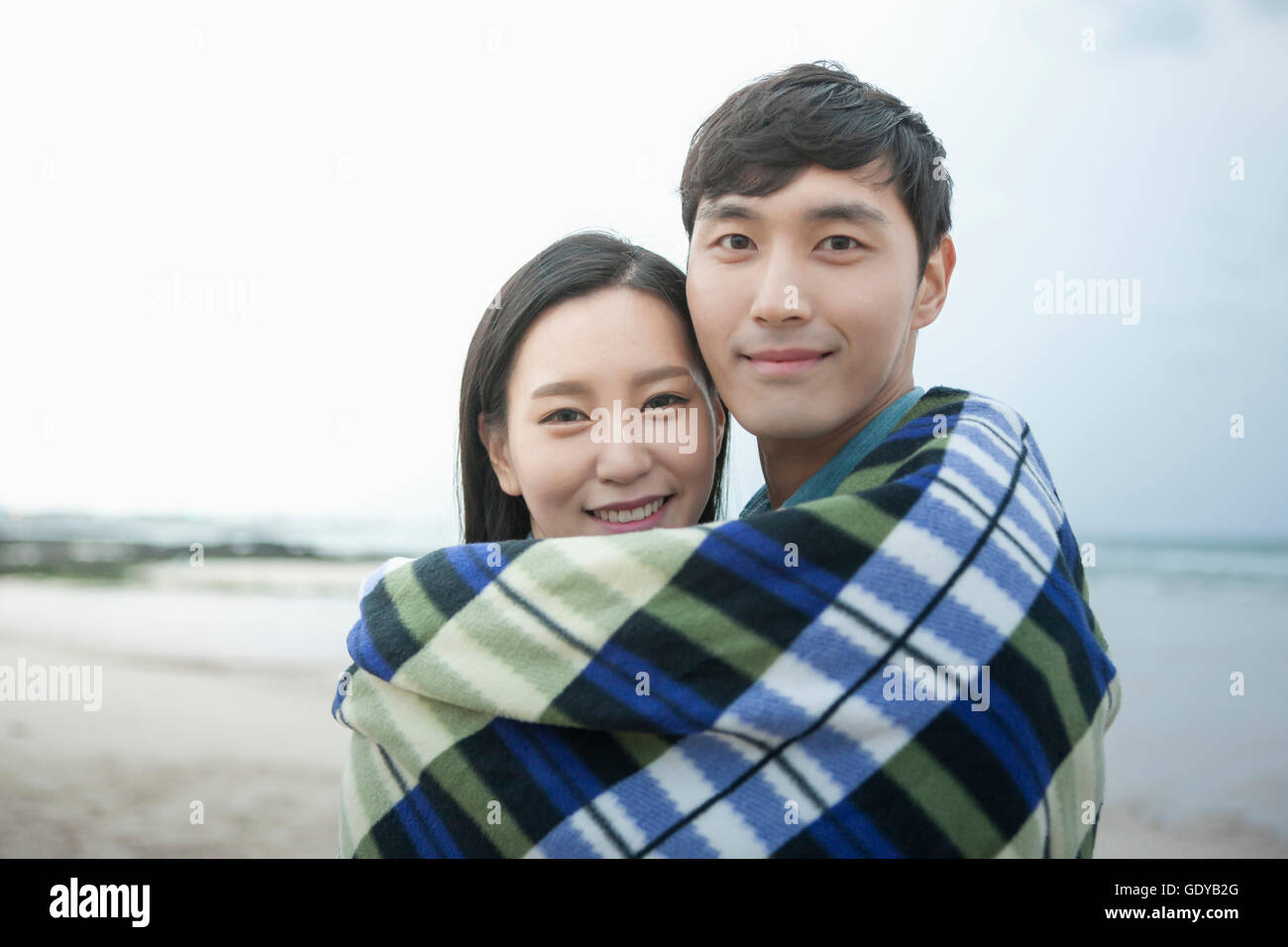 Portrait or young smiling couple sharing a blanket on beach Stock Photo ...