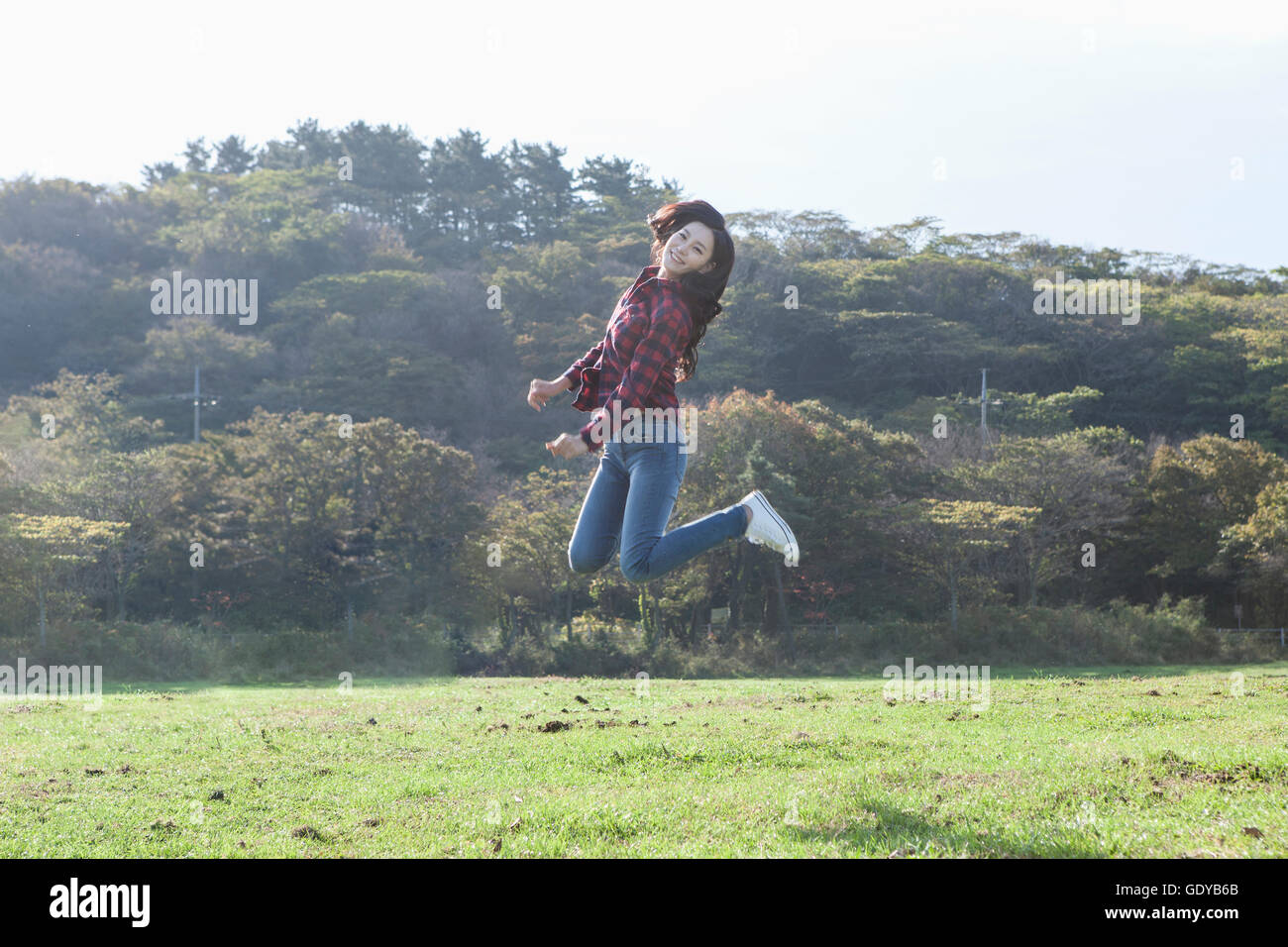 Side view of young smiling woman jumping in field Stock Photo - Alamy