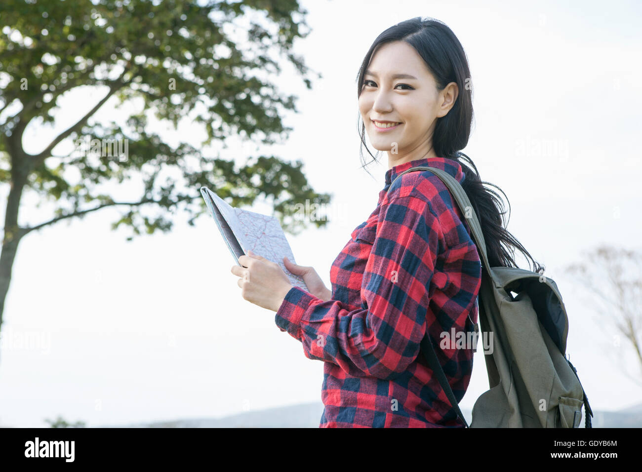 Side view portrait of young smiling female backpacker holding a map ...