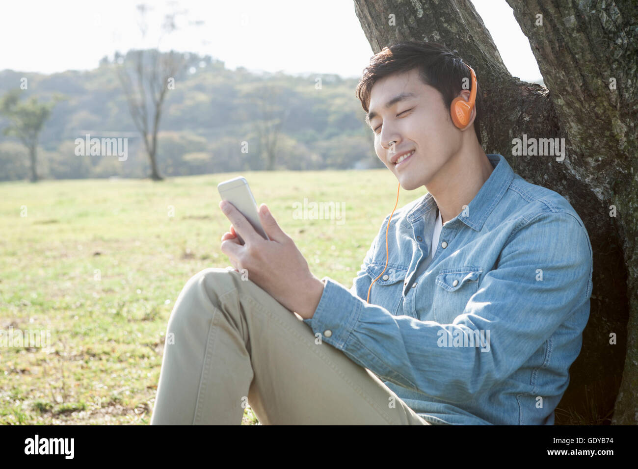 Side view of young smiling man listening to music closing eyes under a ...
