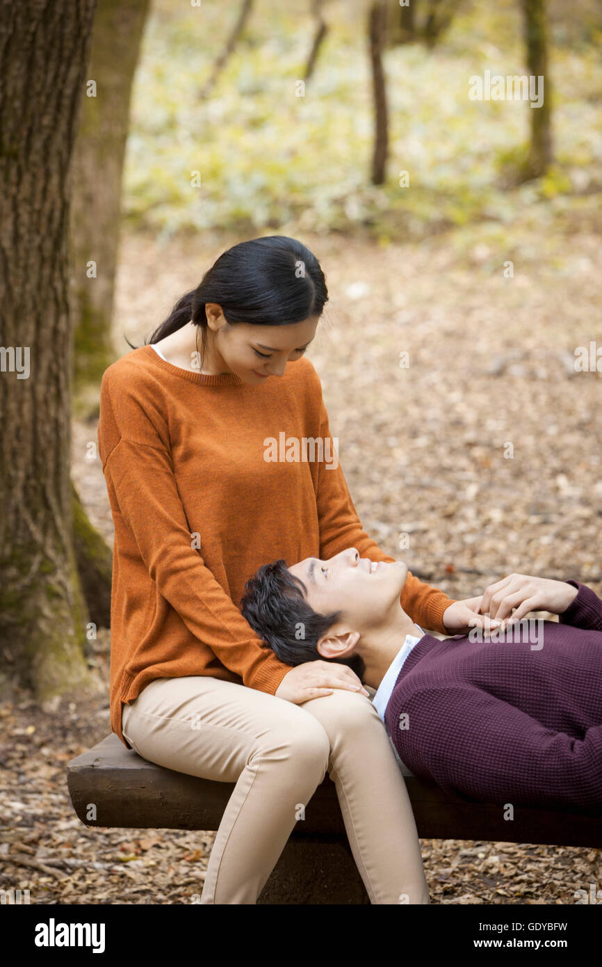 Young smiling couple having a date on bench in forest in fall face to ...