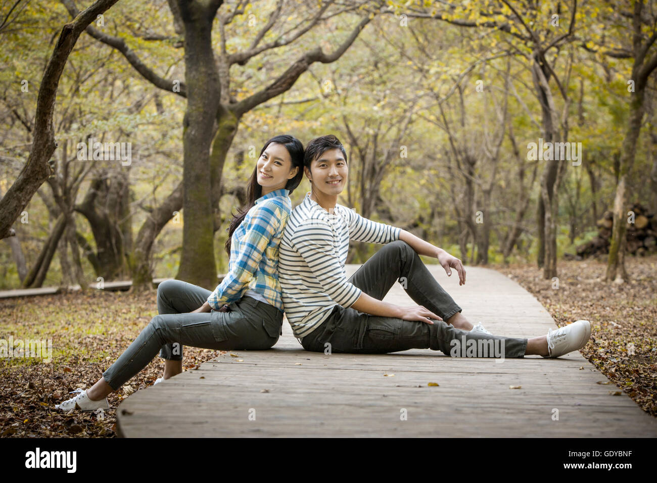 Side view of young smiling couple sitting back to back in park staring ...