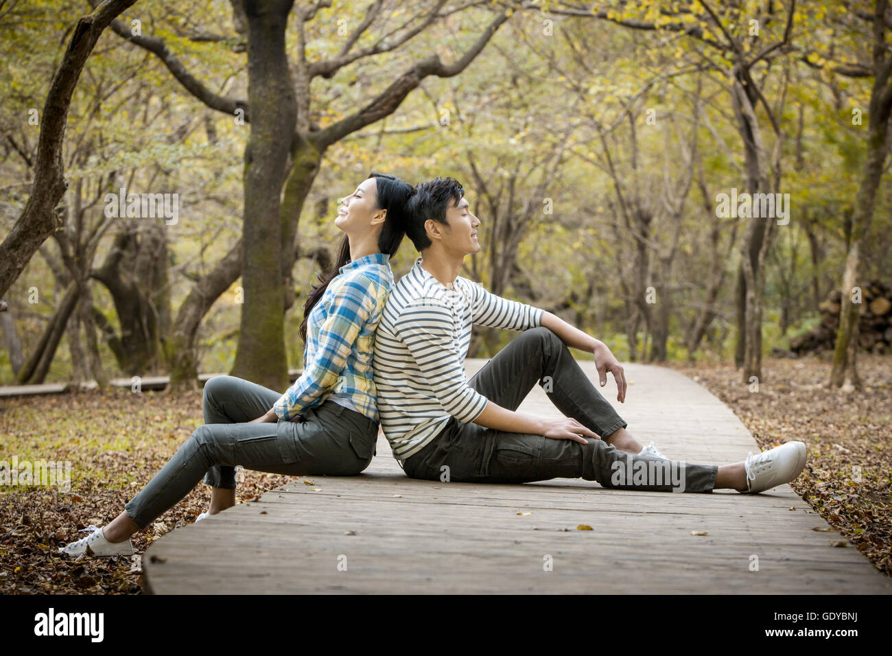 Side view of young smiling couple sitting back to back in park Stock ...
