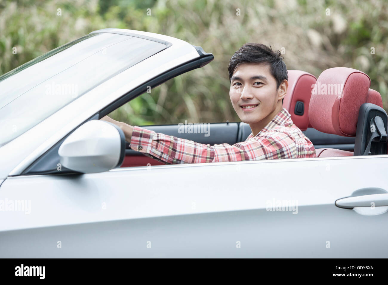 Side view portrait of young smiling man driving a car staring at front ...