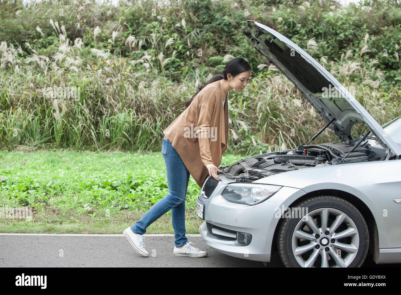 Side view of young woman standing and checking her car Stock Photo - Alamy