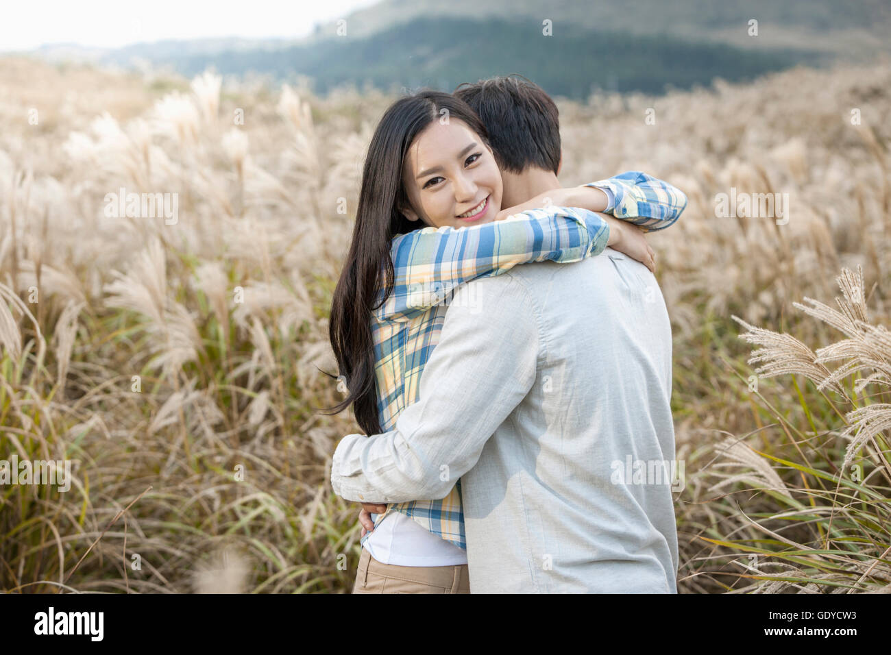 Side view of young smiling woman hugging with a man in silver grass ...