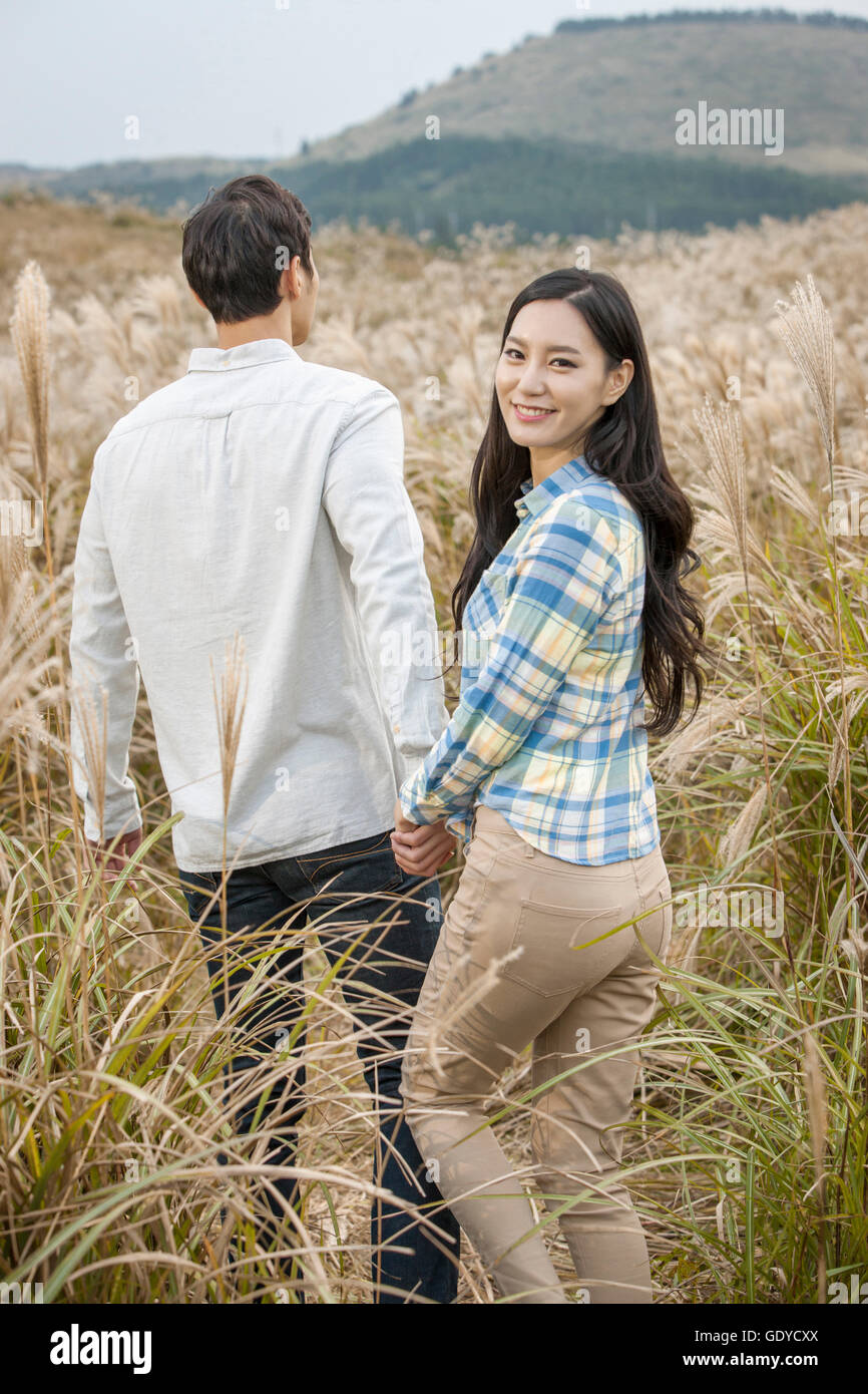 Young smiling woman looking back while walking holding hands with a man ...