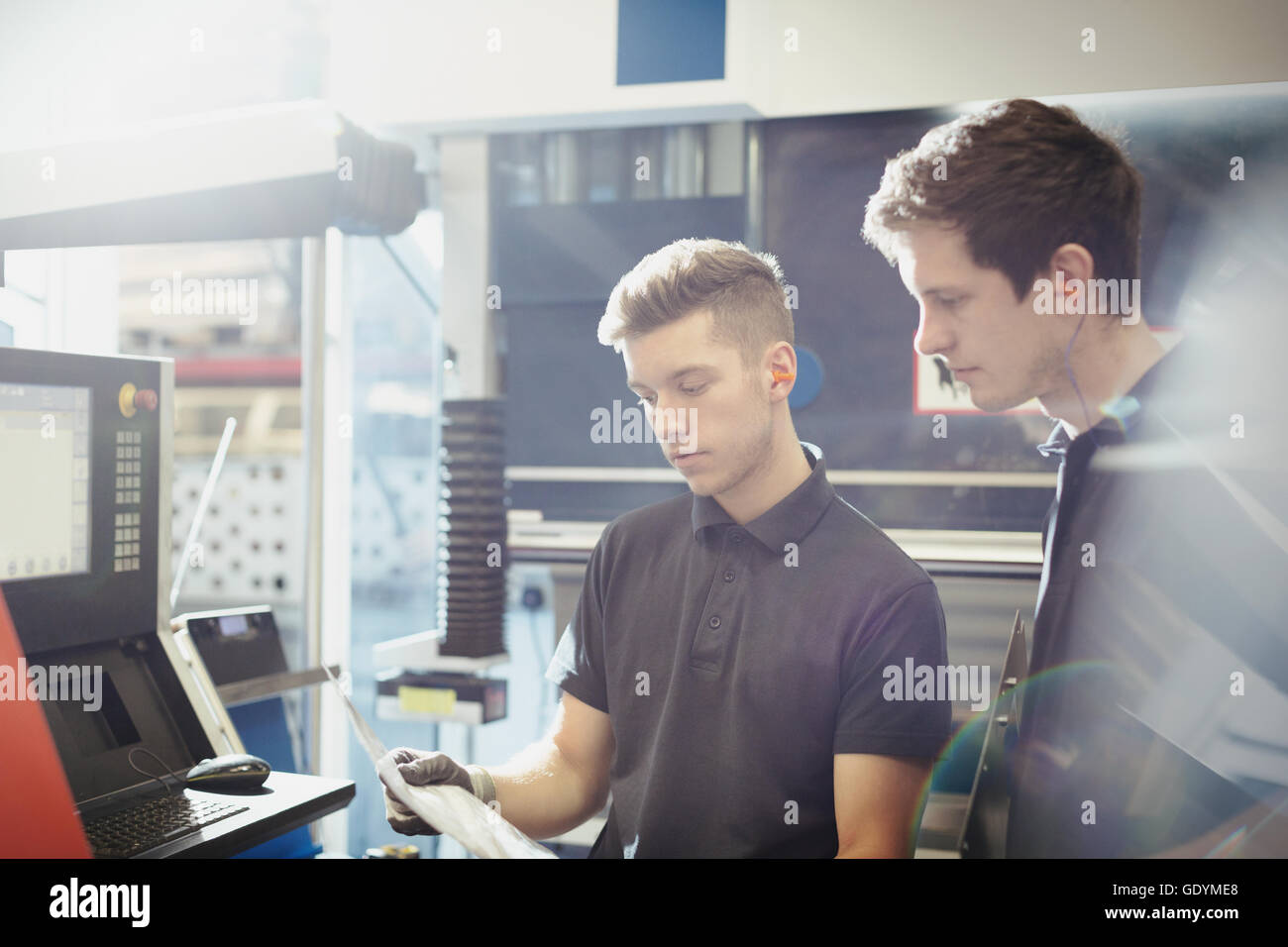 Workers reviewing paperwork at machinery control panel in steel factory ...