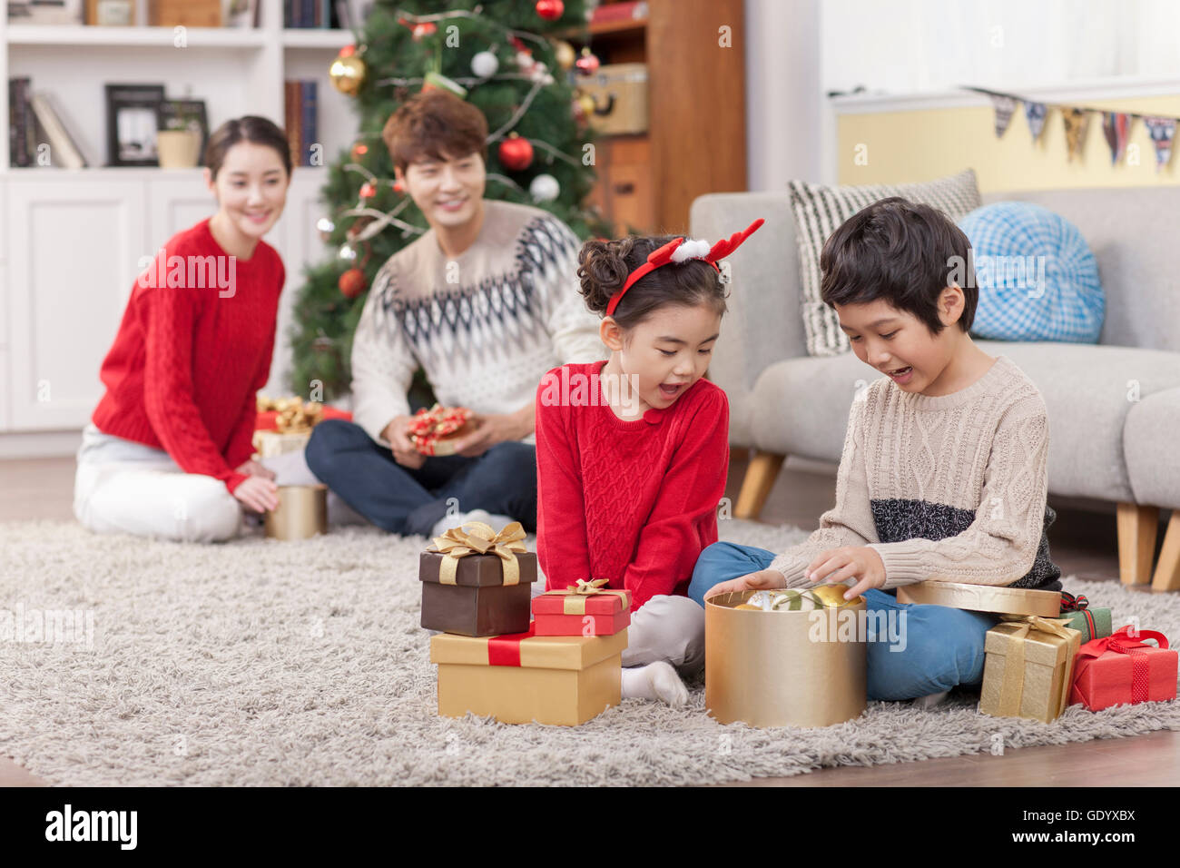 Boy and girl delighted with Christmas present boxes and their parents ...