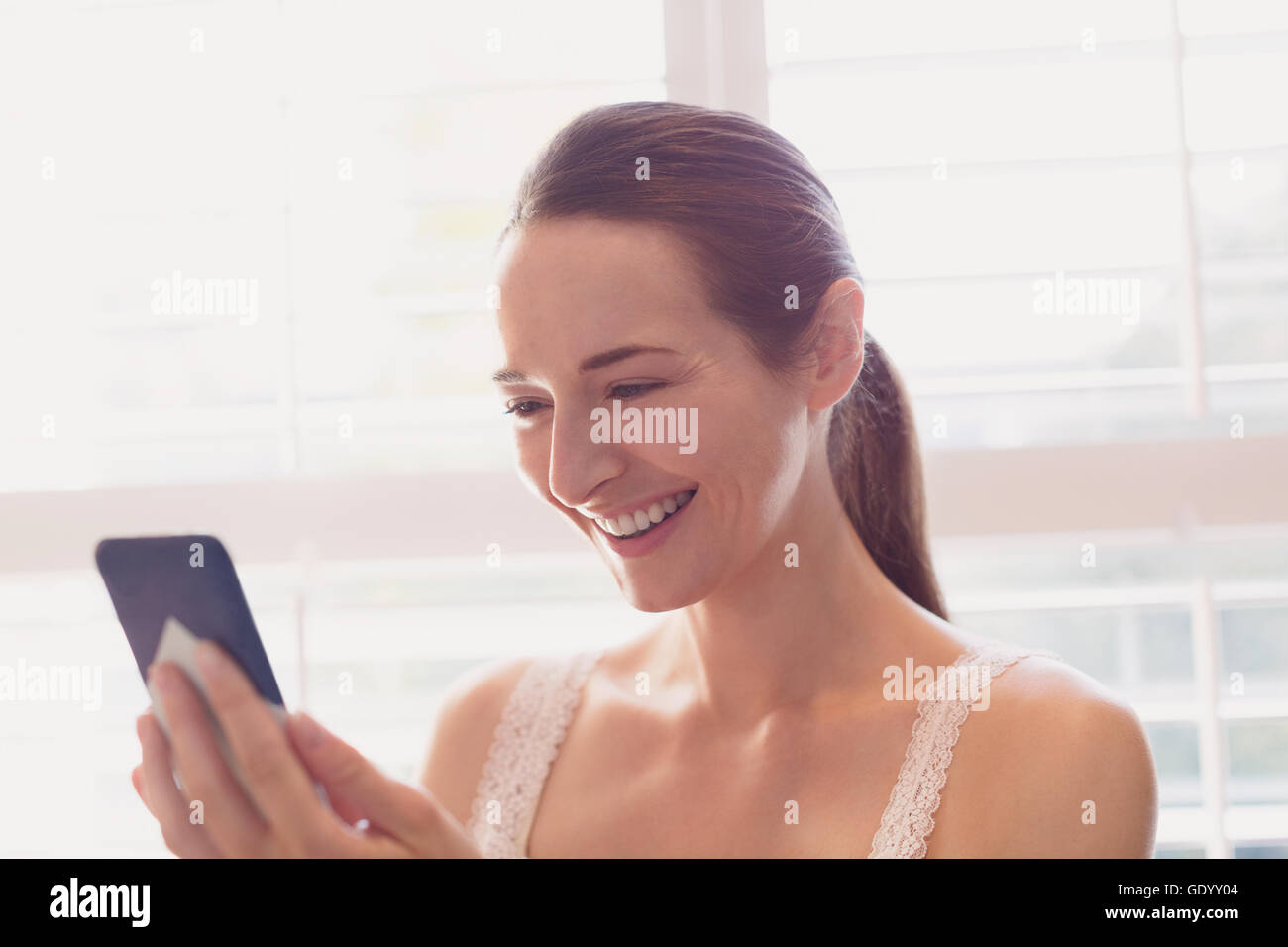 Smiling woman texting with cell phone at window Stock Photo - Alamy