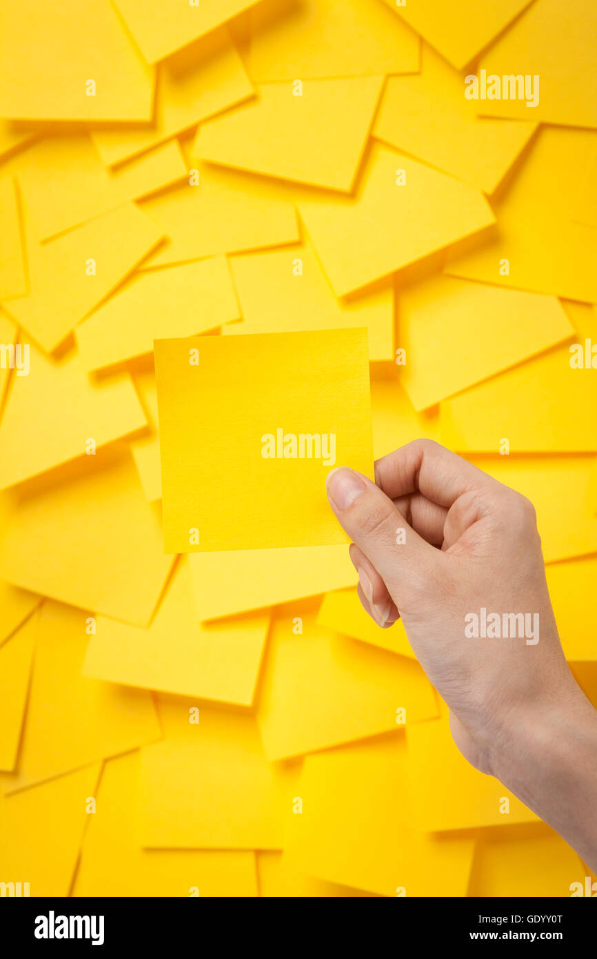 Hand holding a piece of post-it against lots of ones Stock Photo - Alamy
