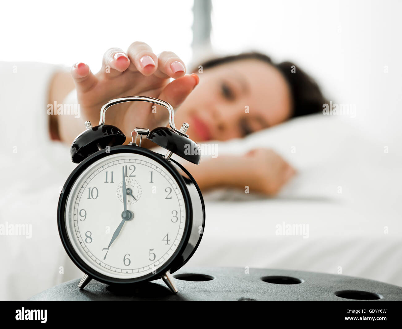 Beautiful young woman waking up with the alarm clock Stock Photo - Alamy