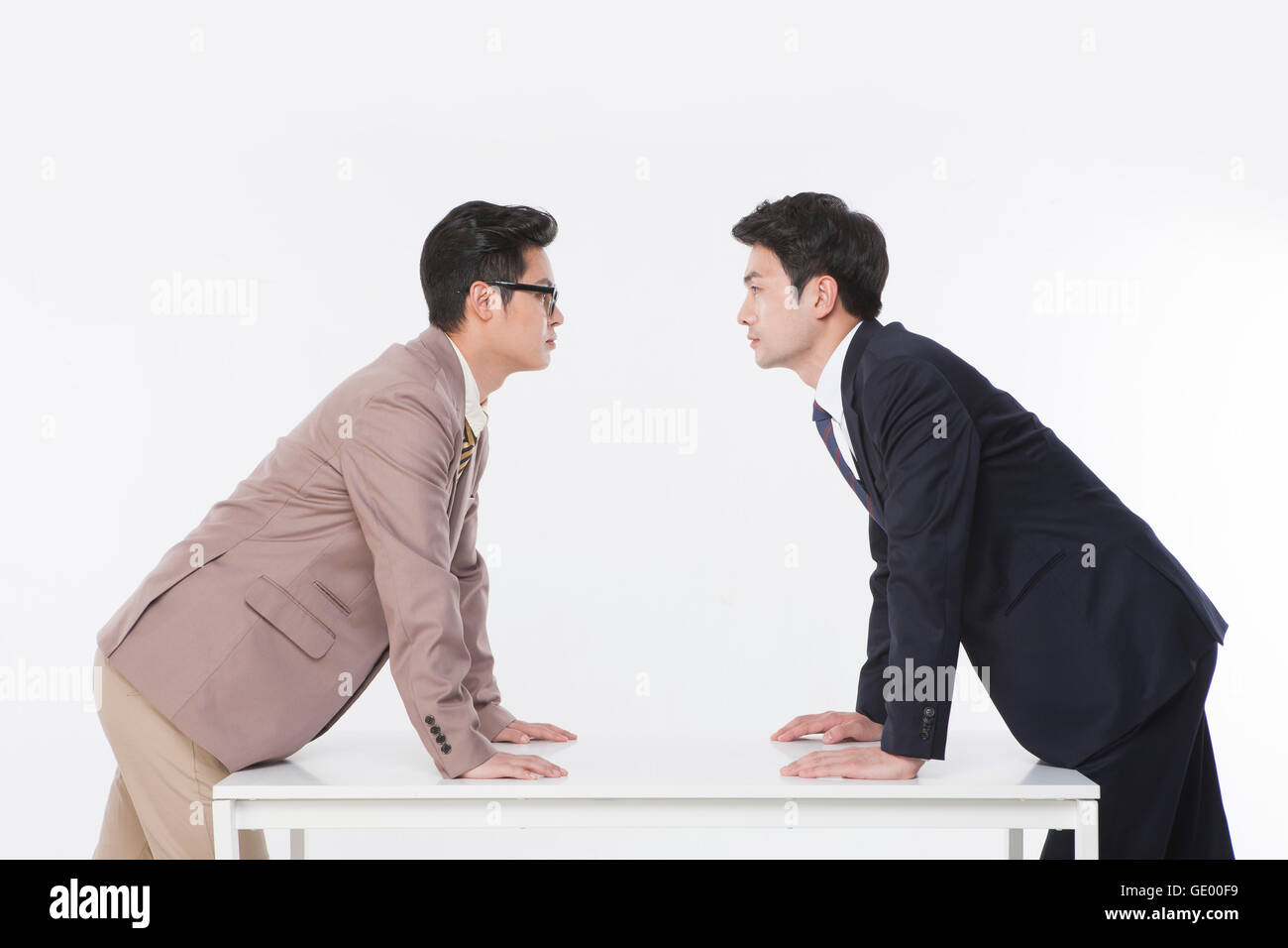 Side view of two businessmen in suits standing face to face at table ...