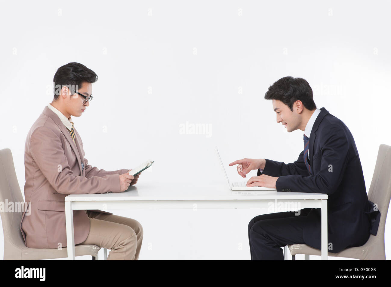 Side view of two business men sitting at table with a book and a ...