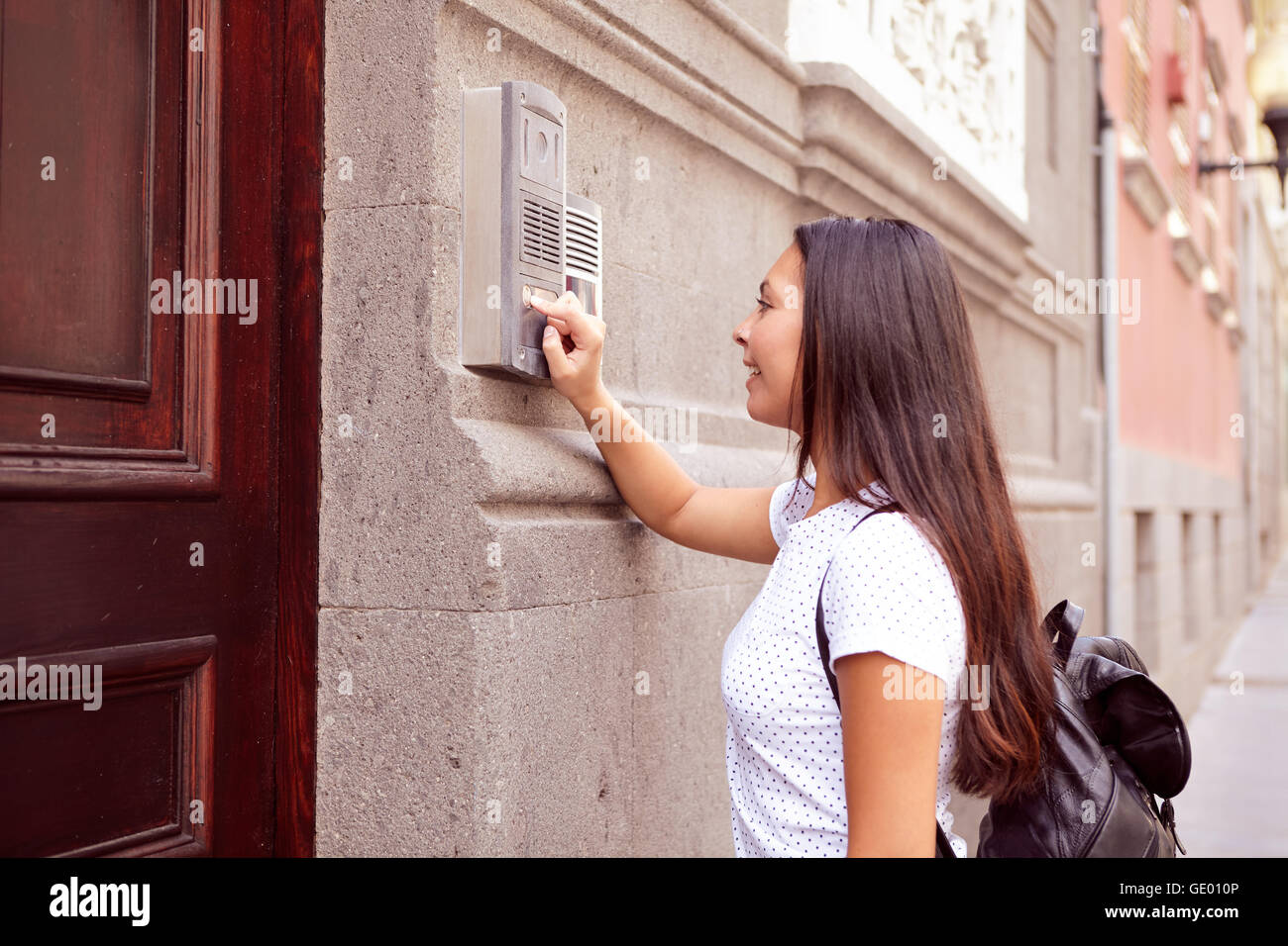 Pretty visiting girl with a back pack buzzing the intercom at a wooden ...