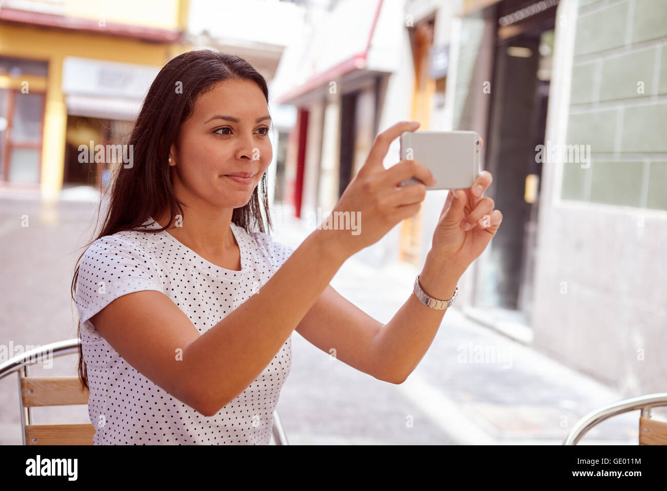 Secretively smiling young girl in a street cafe taking pictures while ...