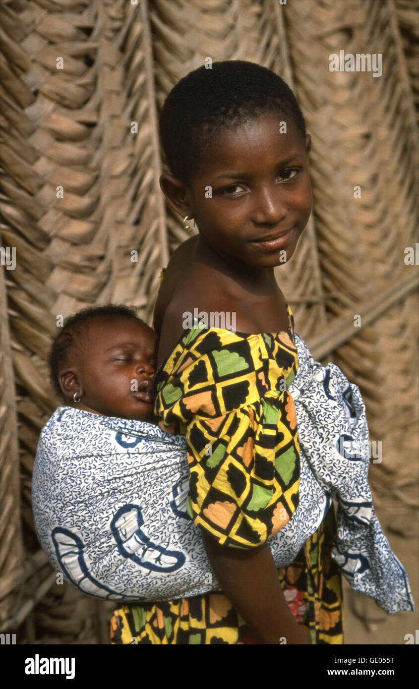 A young Ewe girl carries her sister on her back in the fishing ...
