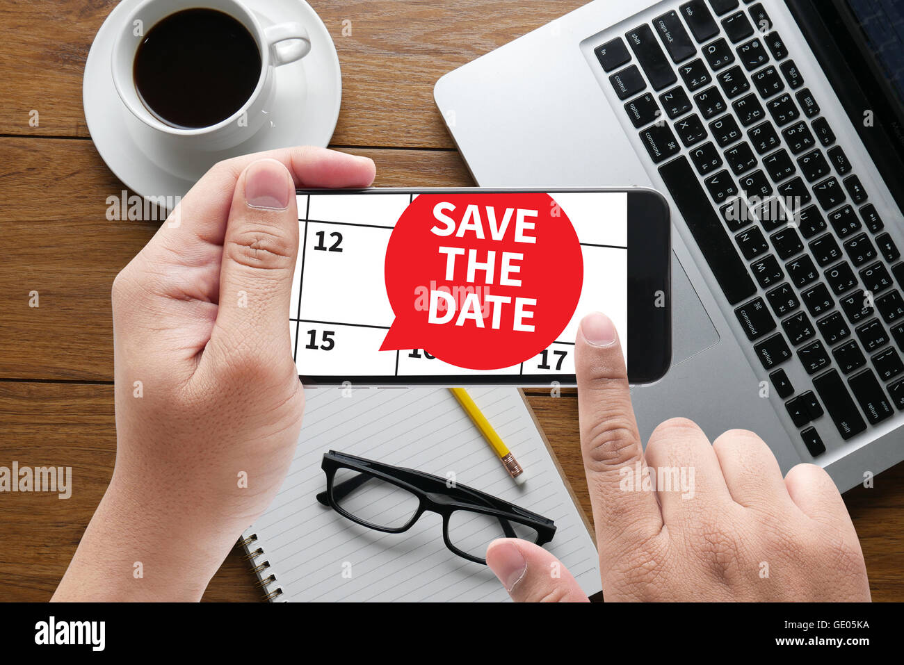 SAVE THE DATE message on hand holding to touch a phone, top view, table ...