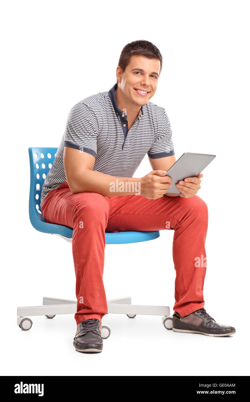 Vertical shot of a young man holding a tablet and sitting on a chair ...