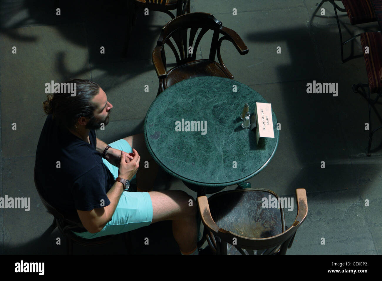 Looking down on a male seated alone at an empty table in a restaurant ...
