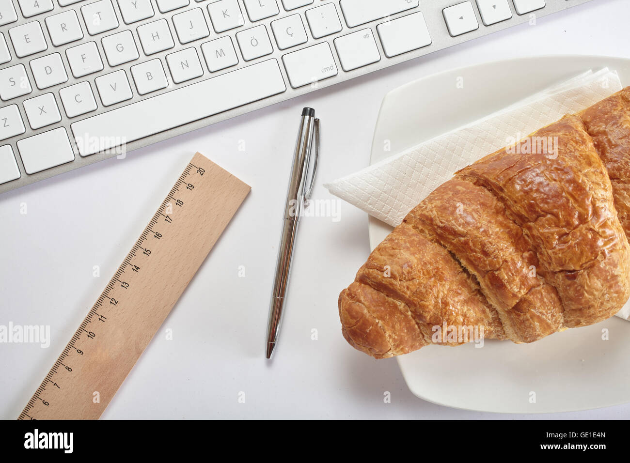 Top view office workplace - keyboard, pen, ruler and croissant on white ...