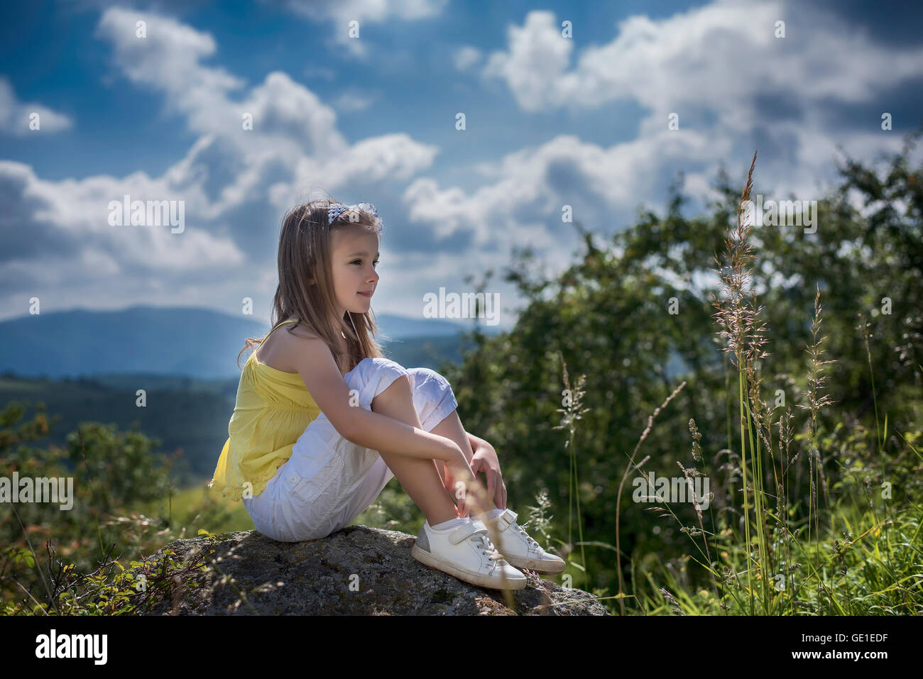 Girl sitting on a rock looking at view Stock Photo - Alamy