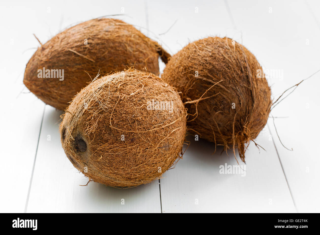 Three whole not split coconuts, on a wooden white plank background ...