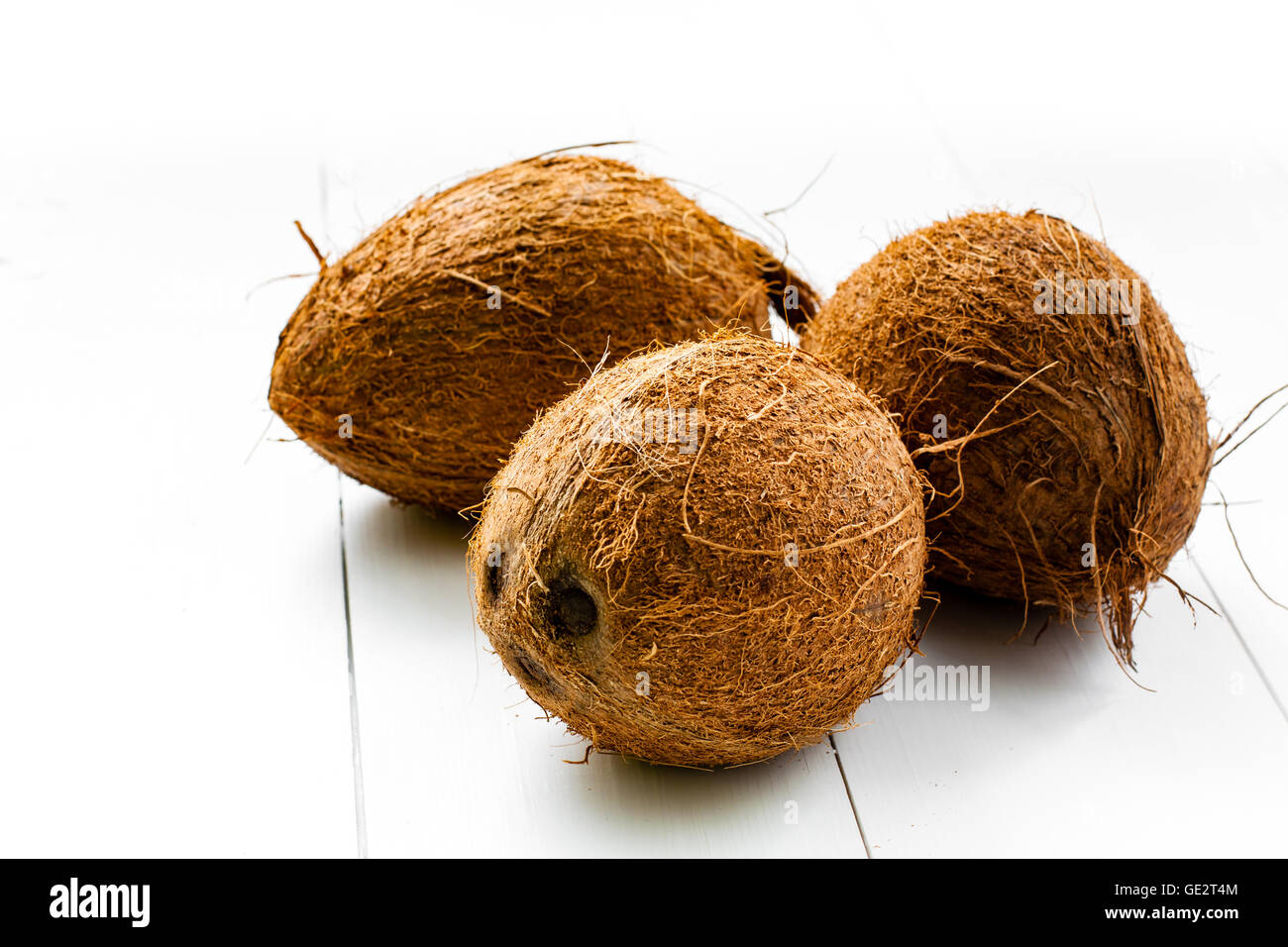 Three whole not split coconuts, on a wooden white plank background ...