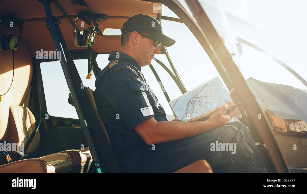 Male pilot sitting in the cockpit of a helicopter and reading flight ...
