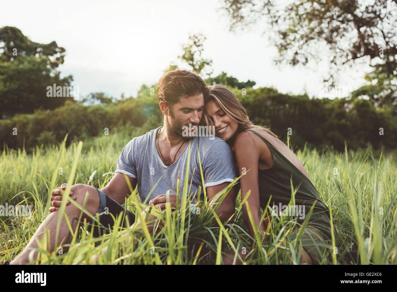 Shot of young man and woman sitting together outdoors on grass field ...