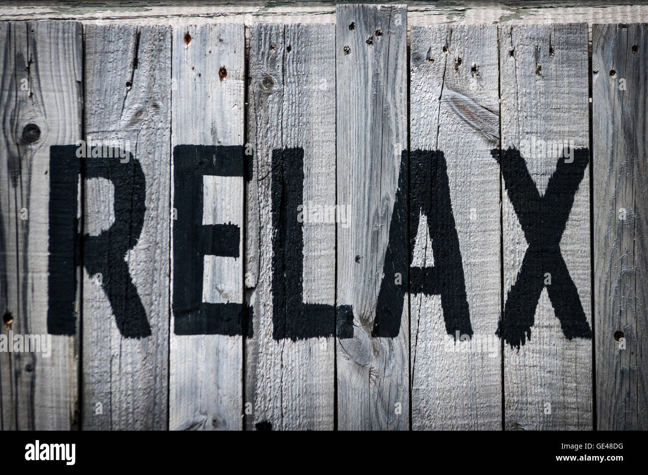 The word relax stencilled on weathered wood in black Stock Photo - Alamy