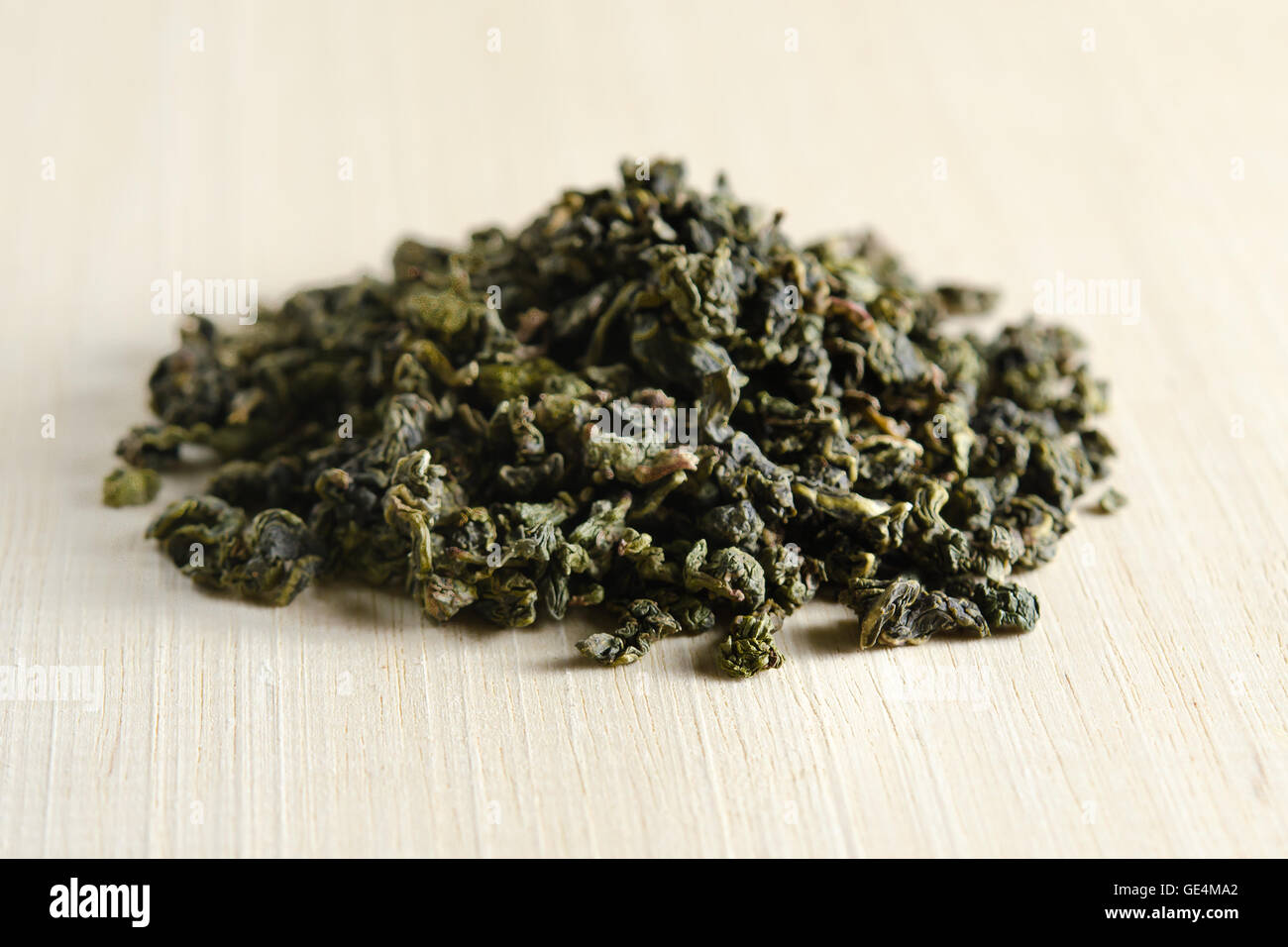 Piles of dried green tea leaves isolated on wooden board background ...