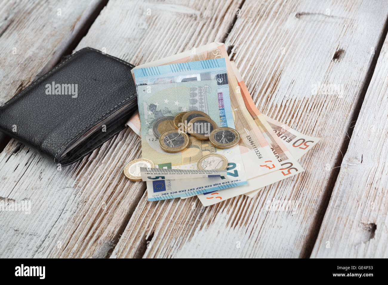 Euro paper currency and coins outside of a wallet on a wooden table ...