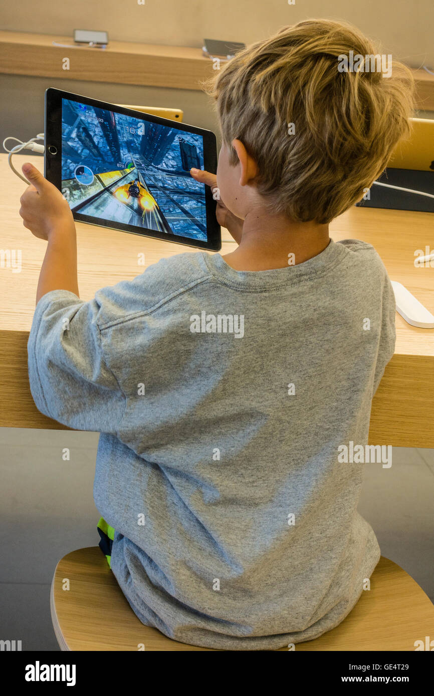 A young boy 7-8 years old plays a game on an iPad at the Apple Store in ...