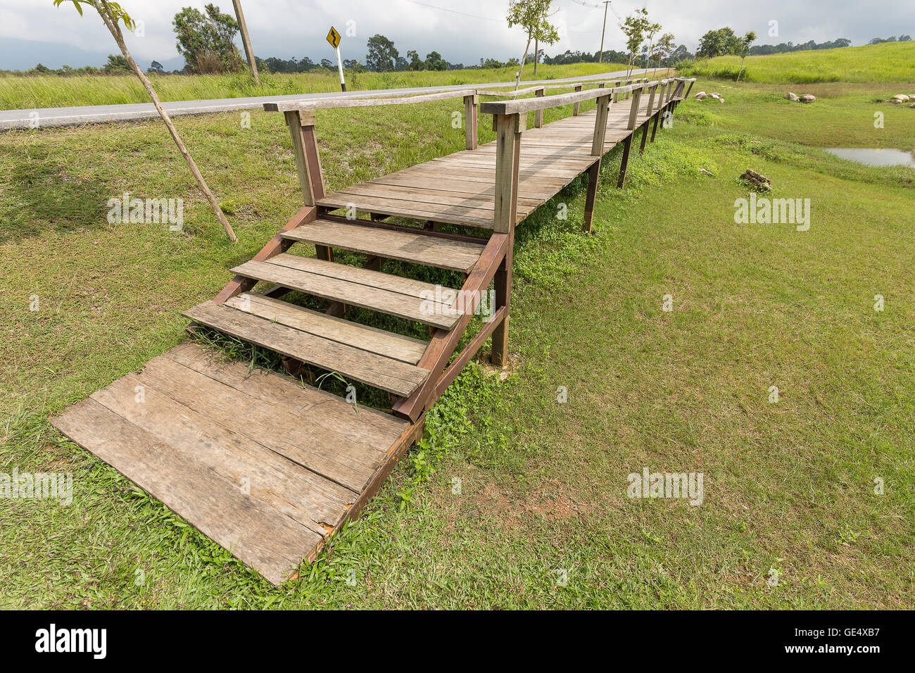 Side view of wooden bridge in green field of grass near small road ...