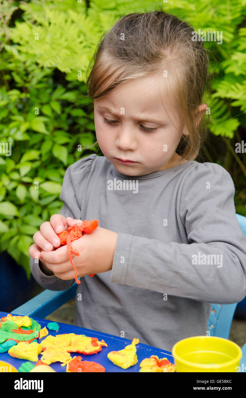 Three year old girl play with Play-Doh modeling putty. UK. Outside in ...