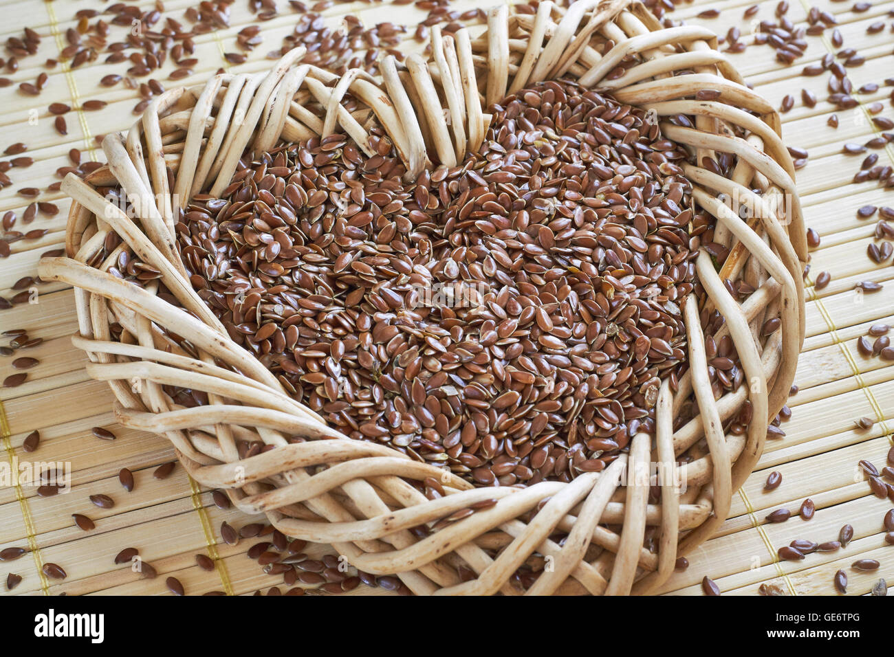 Flax seed in woven heart-shaped basket with flaxseed scattered around on bright wooden ...