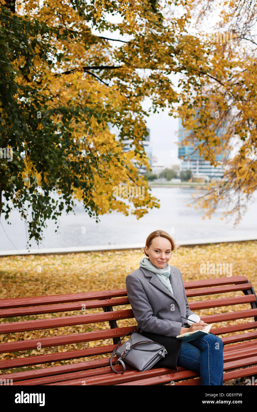 Young blonde woman in elegant clothes sitting under fall foliage in ...