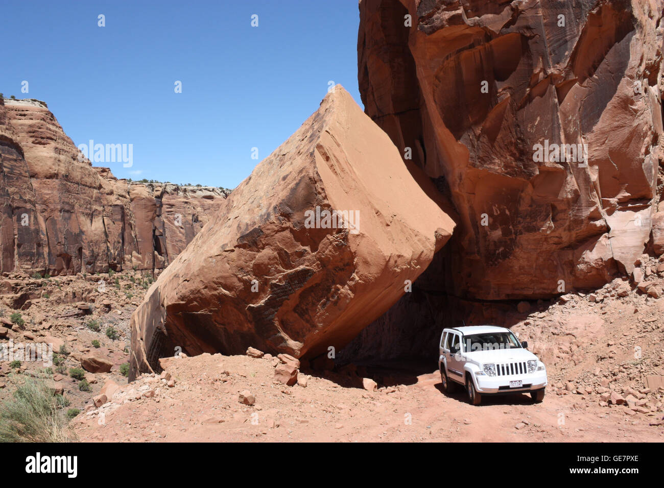 White Jeep drives under massive fallen red rock in Arizona desert ...