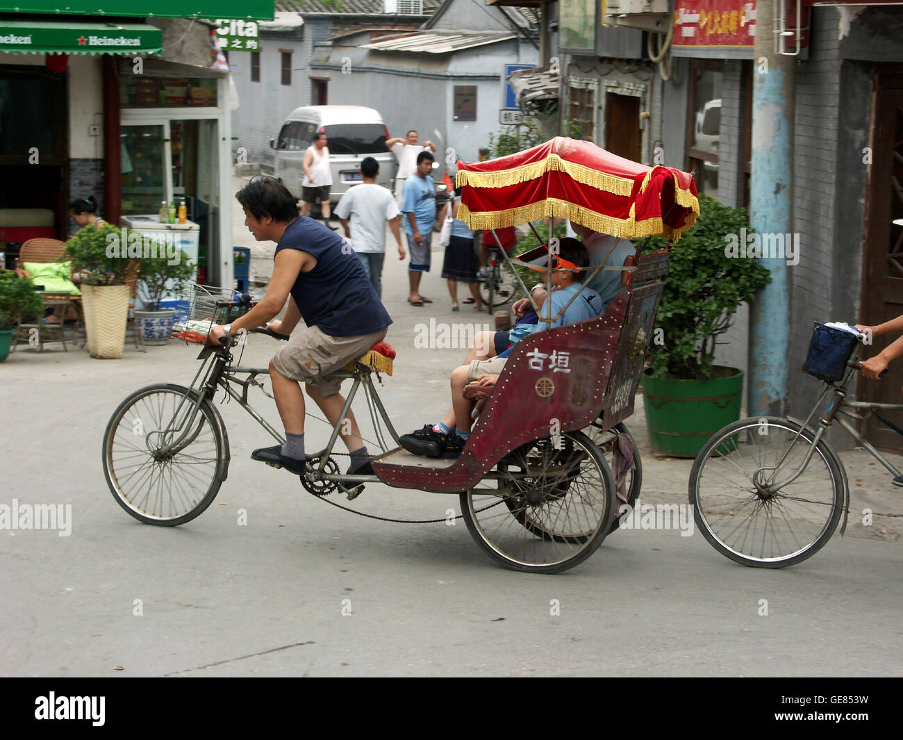 Bicycle rickshaw taking tourists through a hutong neighborhood. Beijing ...