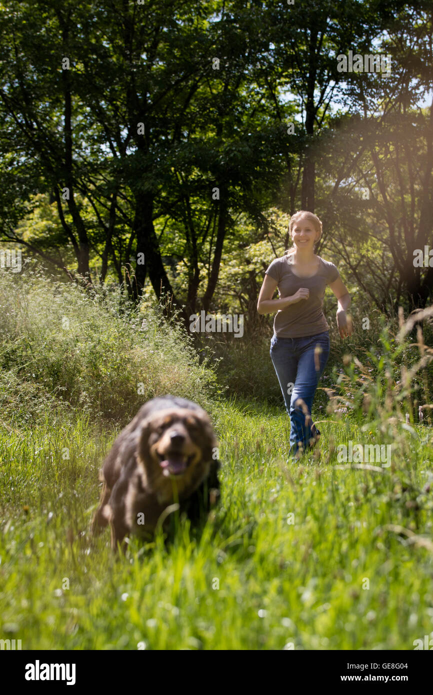 Young woman running after her dog on a meadow Stock Photo - Alamy