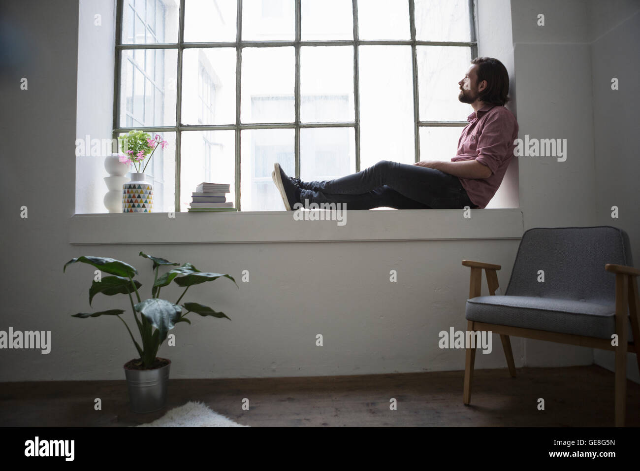 Man sitting on window sill looking out of window Stock Photo - Alamy